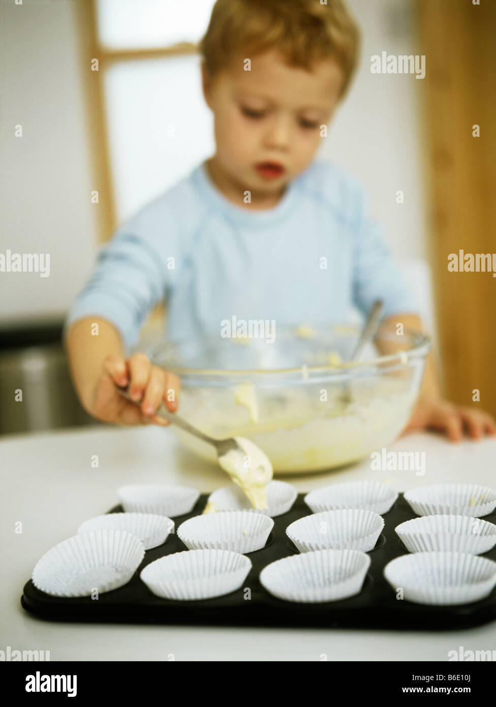 Making cakes. Three year old boy placing cake mixture into individual ...