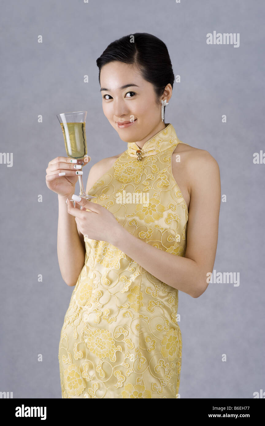 Young woman in a yellow embroidered cheongsam holding a glass of ...