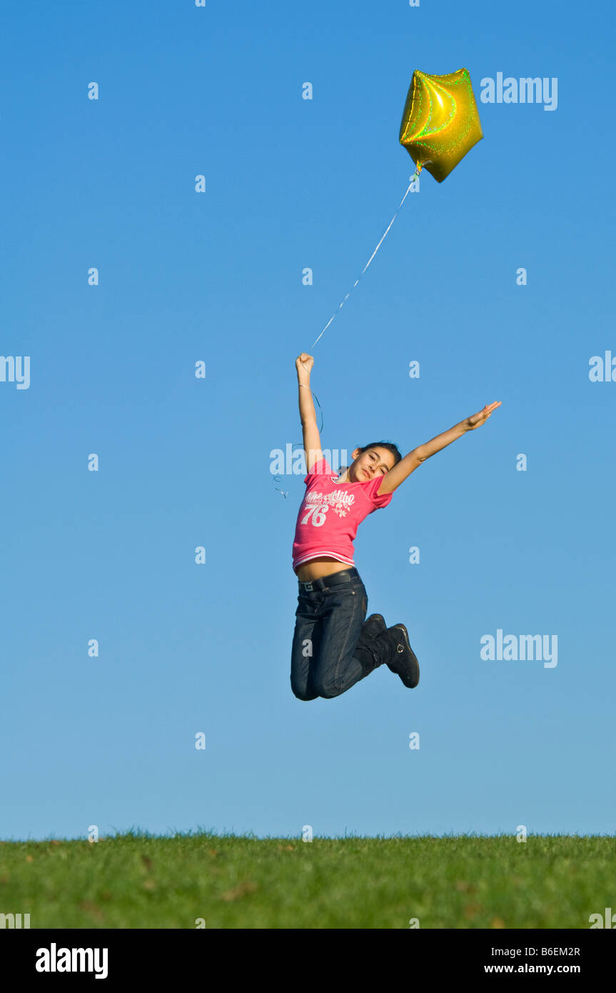 A young girl (11) jumping in the air with a yellow helium filled ...