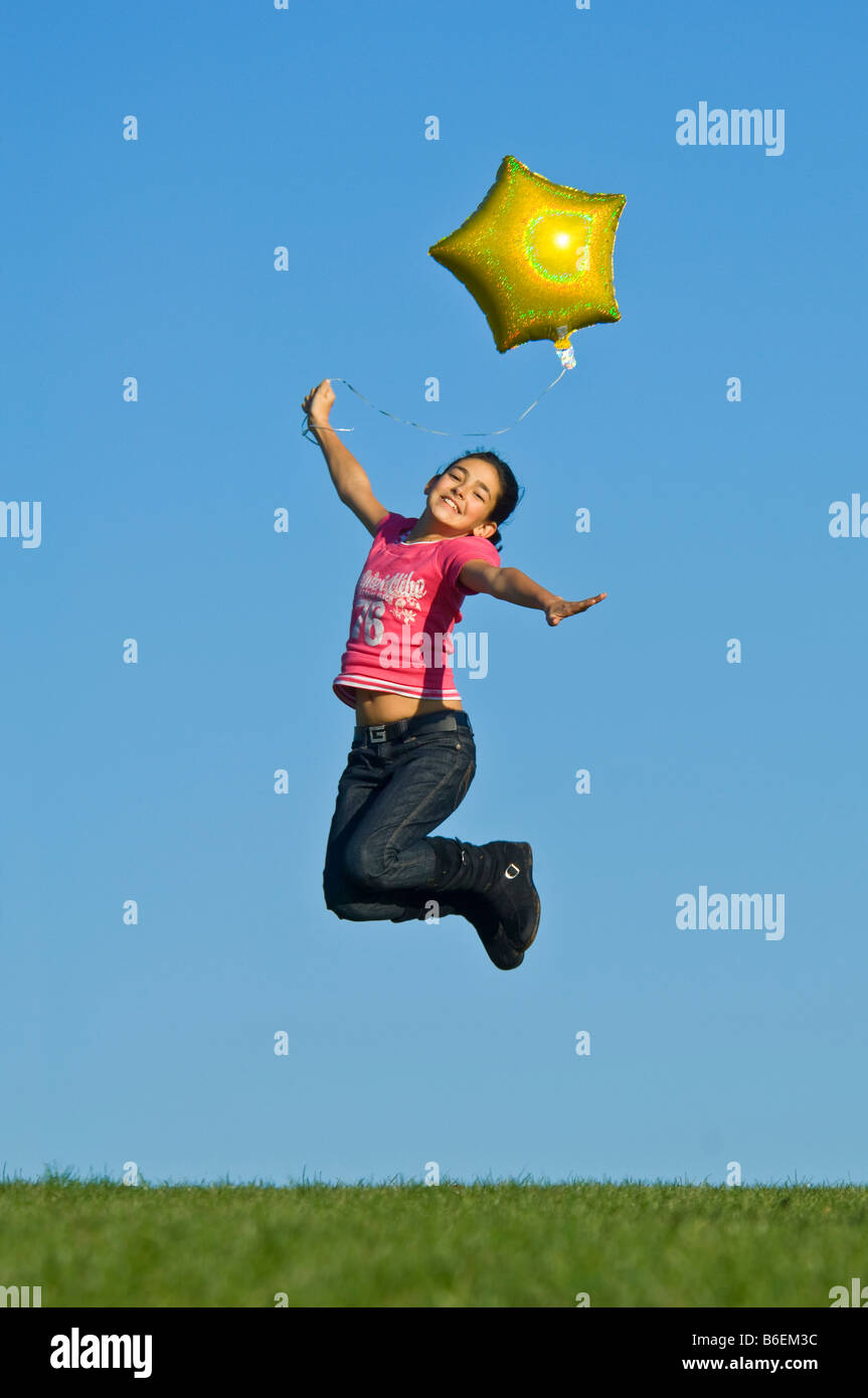A young girl (11) jumping in the air with a yellow helium filled ...