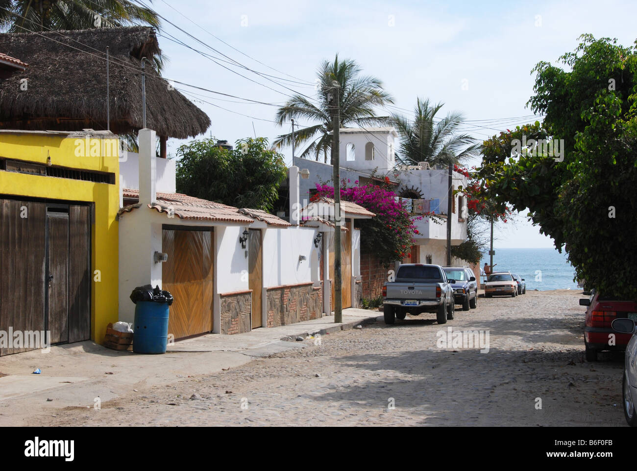 quiet Mexican street with houses, palm trees & a few parked cars ...