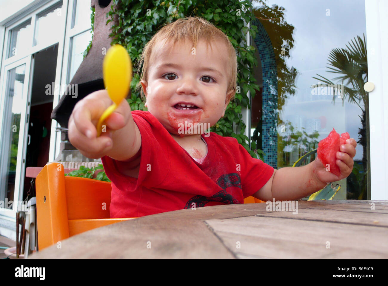 little boy with smudgy mouth in a child seat pointed a spoon towards ...