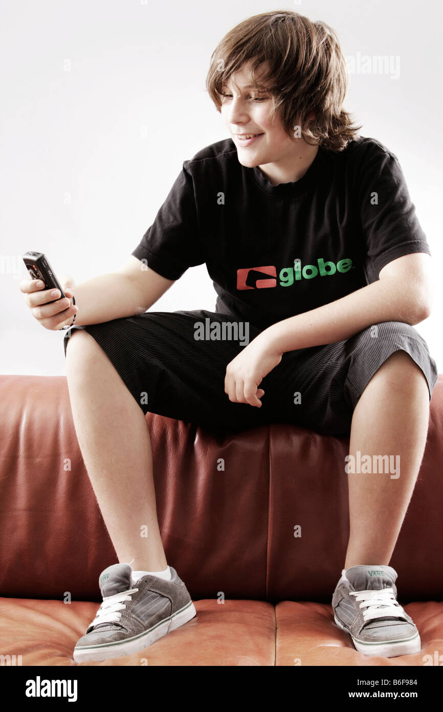 14 year-old boy sitting on a sofa looking at his cellphone, laughing ...