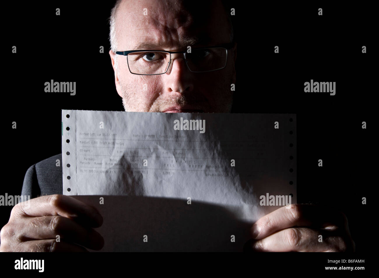 Businessman studying a strip of perforated computer paper, stock quotes ...