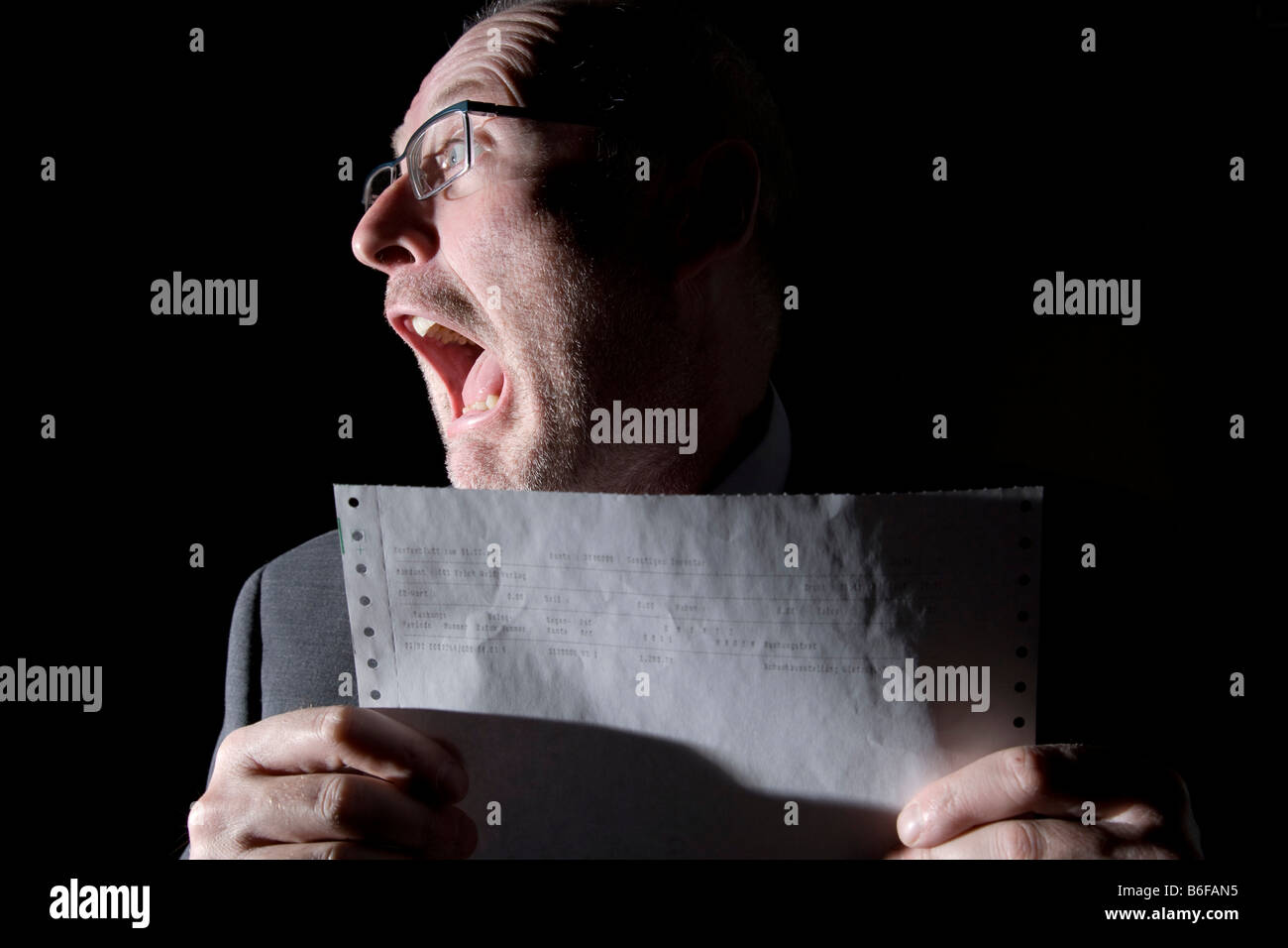 Businessman studying a strip of perforated computer paper, stock quotes ...