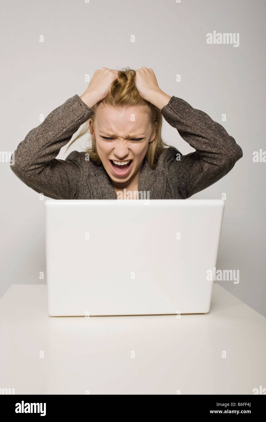 Young long-haired woman yelling in despair at her computer, notebook ...