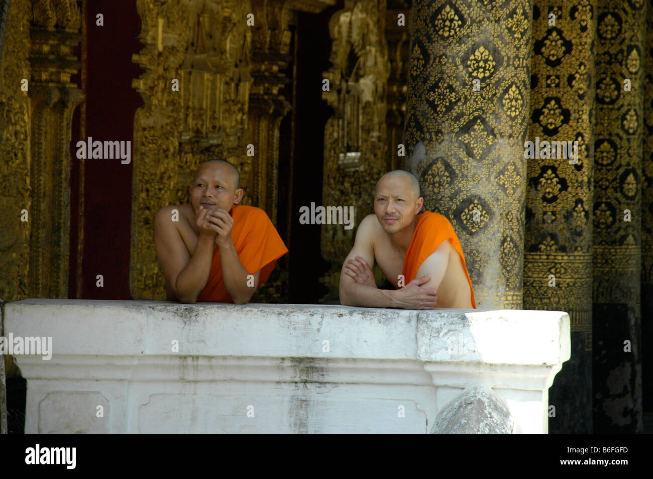 Buddhist monks leaning against a wall of Wat Mai Suwannaphumaham, Luang ...