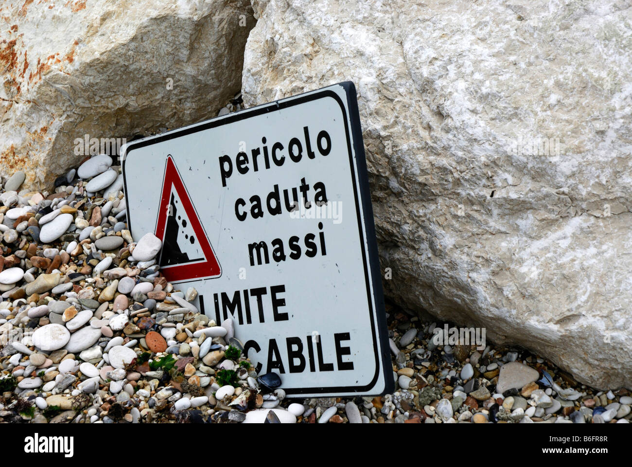 Falling Rock warning sign lying in fallen rock on a beach, Sirolo ...