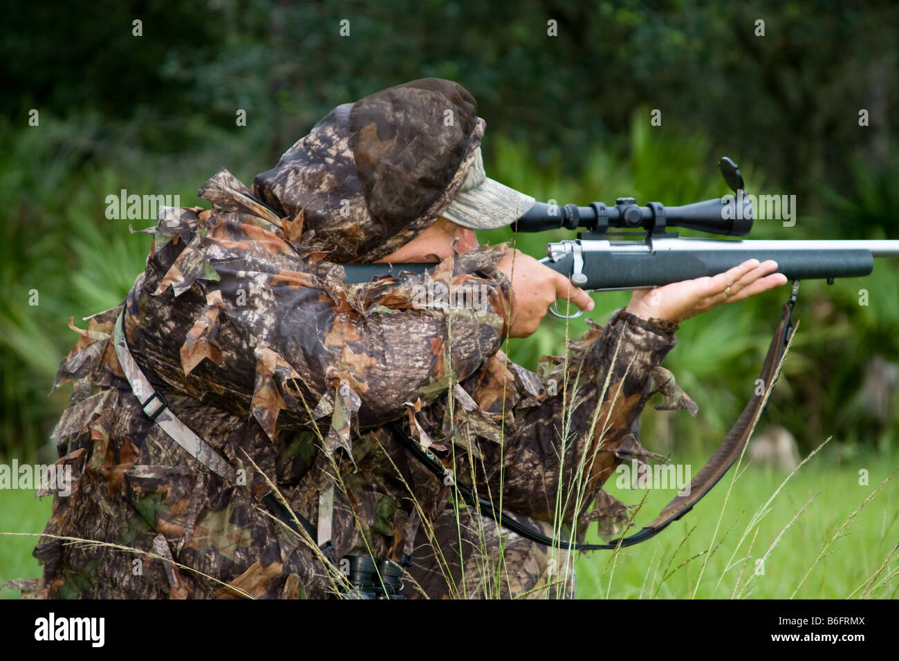 Hunter kneeling in the woods with a high powered rifle taking aim ...