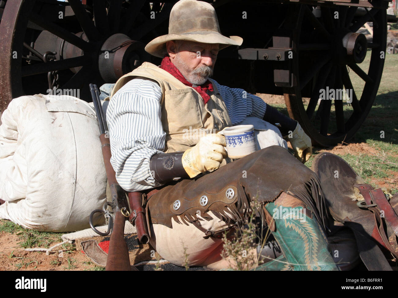 A seasoned cowboy resting against his bedroll next to the chuck wagon ...