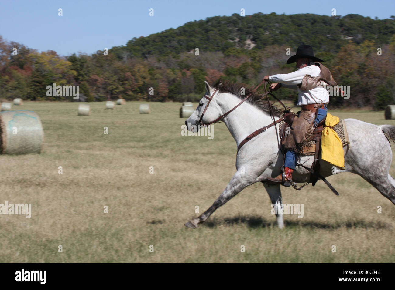 A pan blur of a cowboy galloping full speed in a Texan hayfield in fall ...