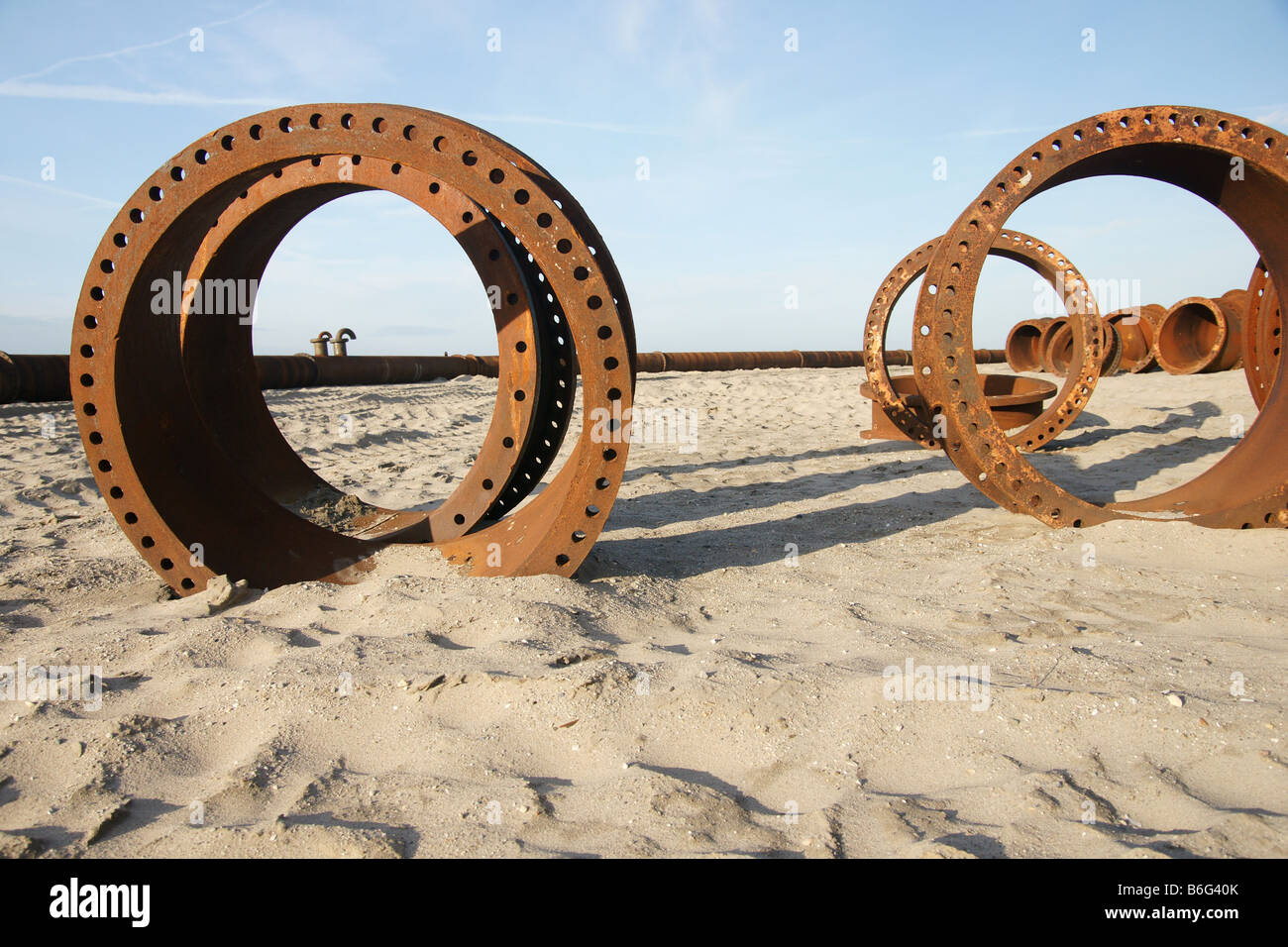 Rusty circular rings pipeline parts partly buried in sand beach with ...