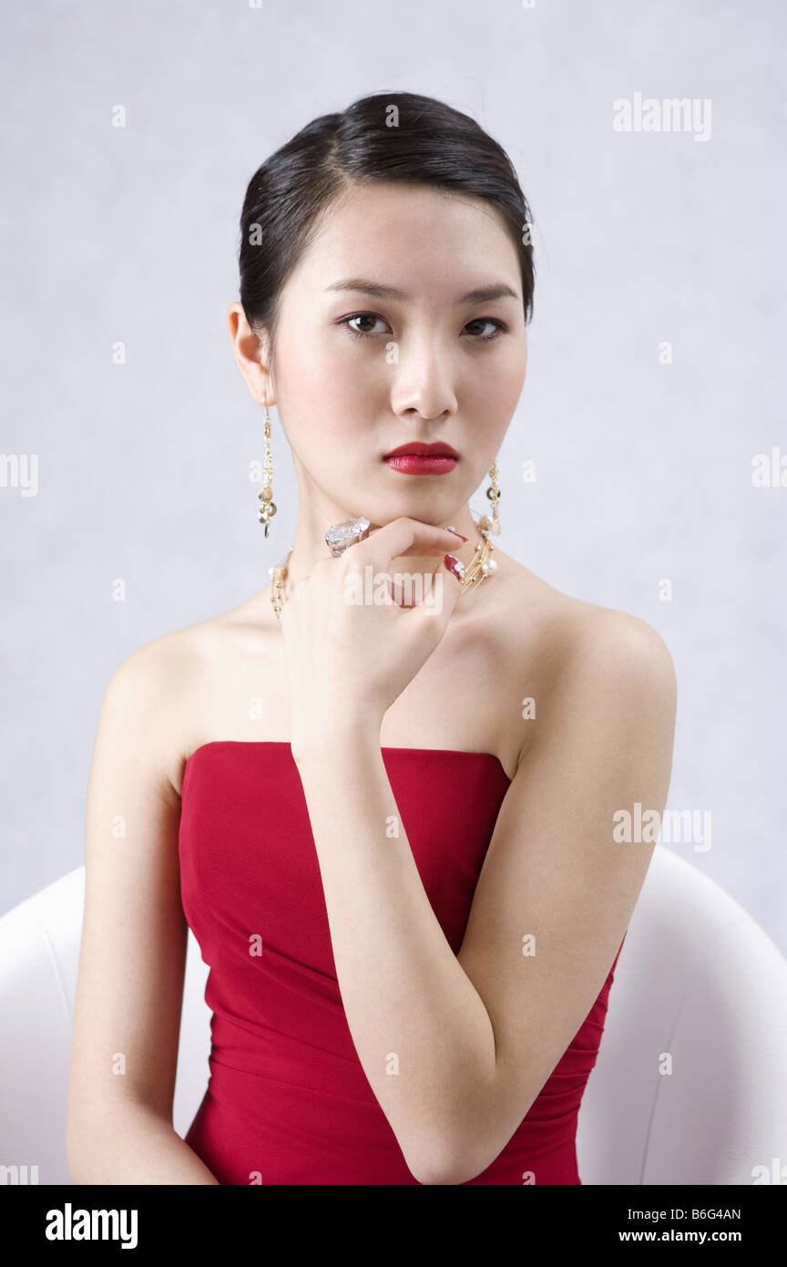 Young woman wearing a red dress and jewelry dressed up hand on chin ...