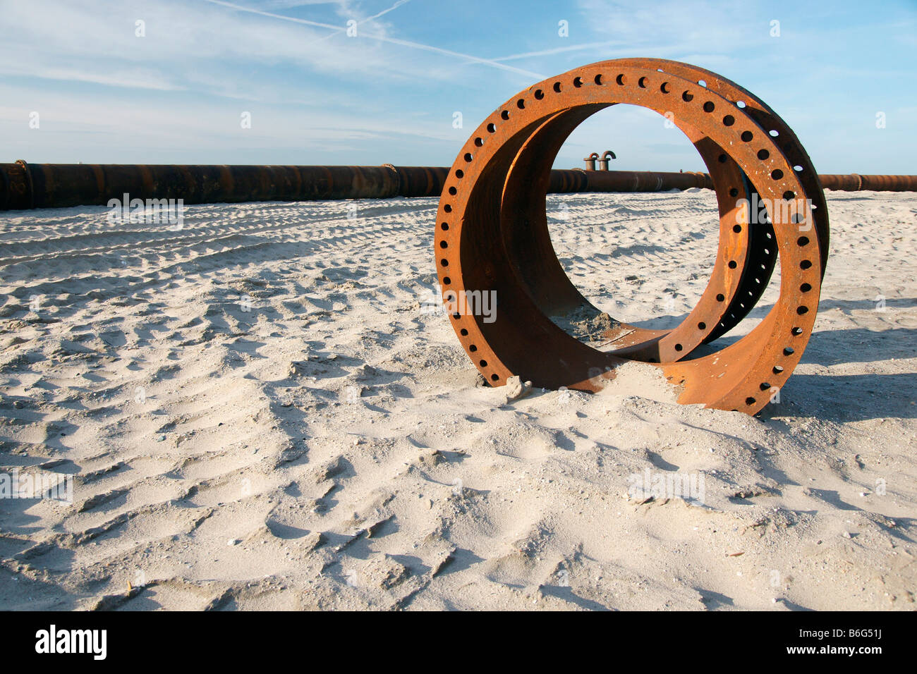 Rusty circular rings pipeline parts partly buried in sand beach with ...