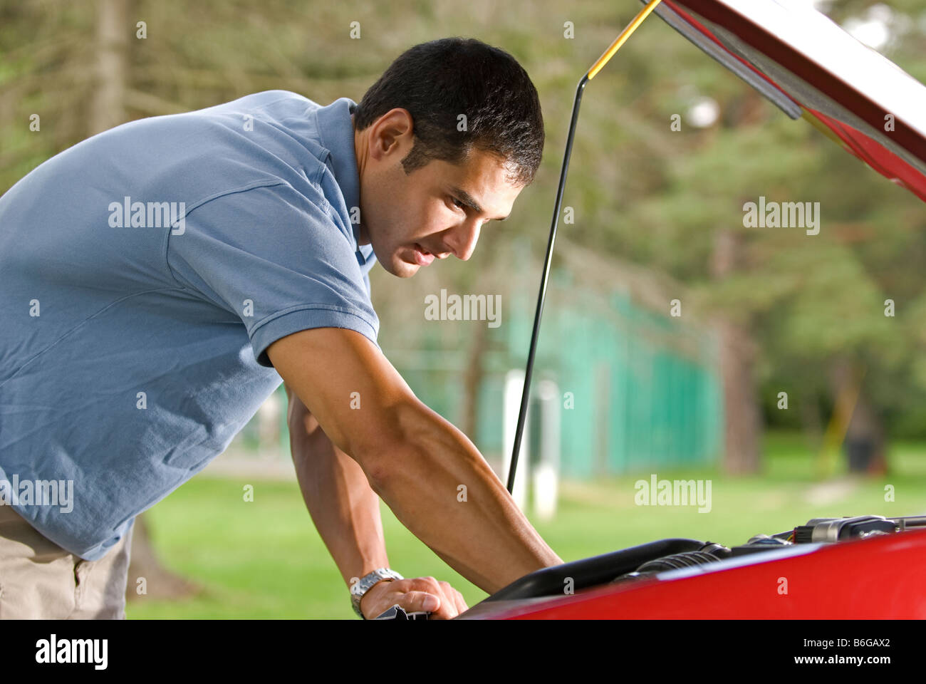 Attractive young man reaching into car engine compartment Stock Photo ...