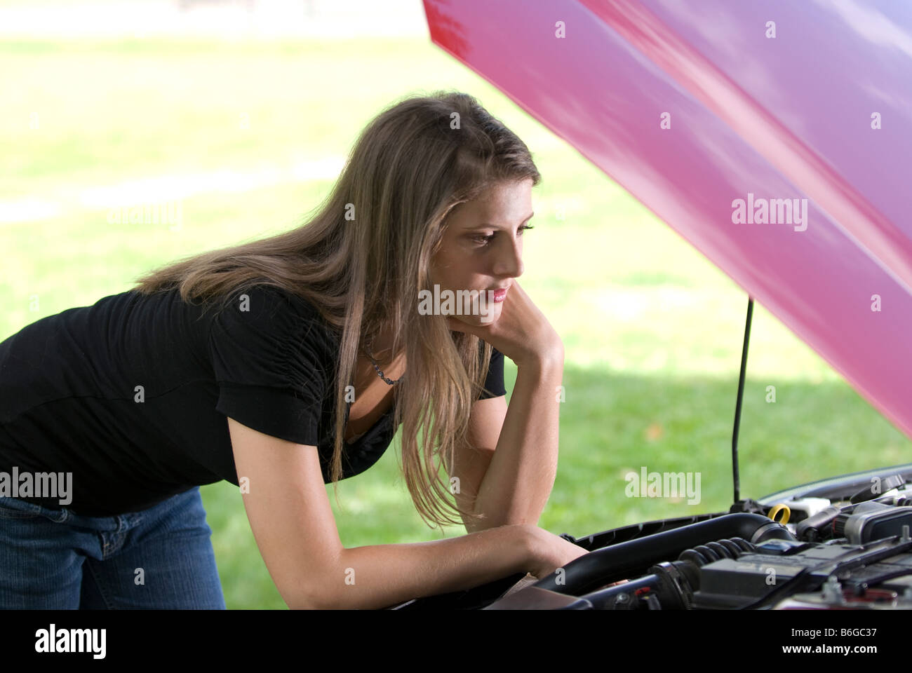 Young woman looking under the hood bonnet of a car appearing confused and perplexed Stock Photo ...