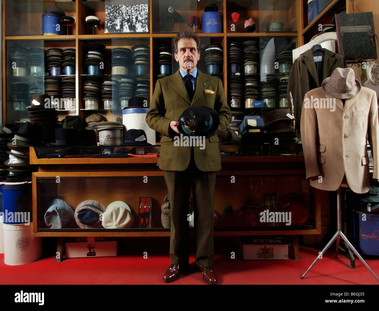 Proprietor of traditional old fashioned hat shop in Rome holding hat ...