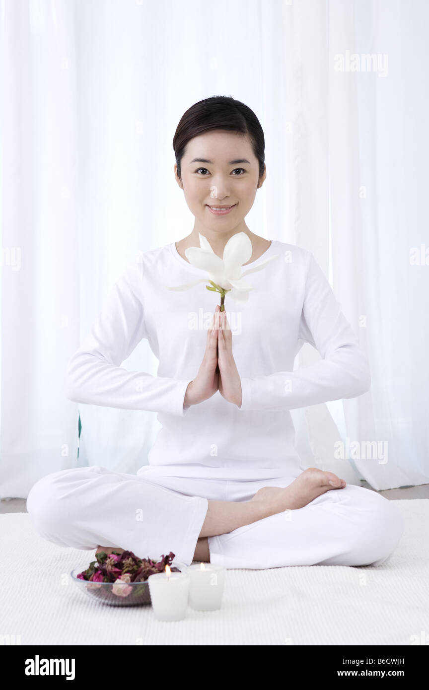 Young woman sitting on a mat in prayer position holding a white lotus ...