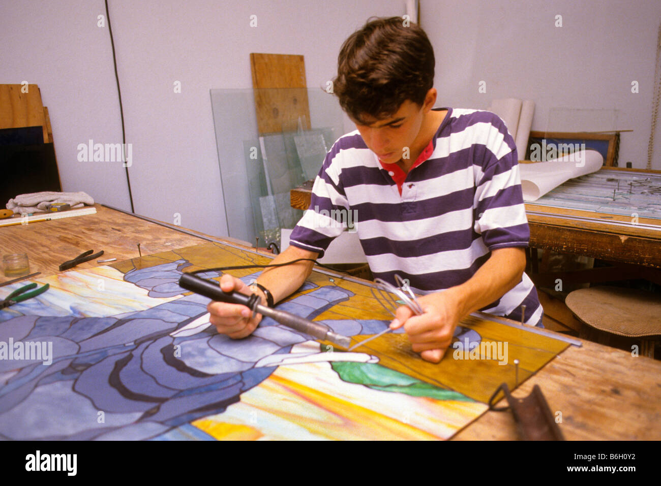 Teen boy creates stained glass window with glass and solder Stock Photo ...