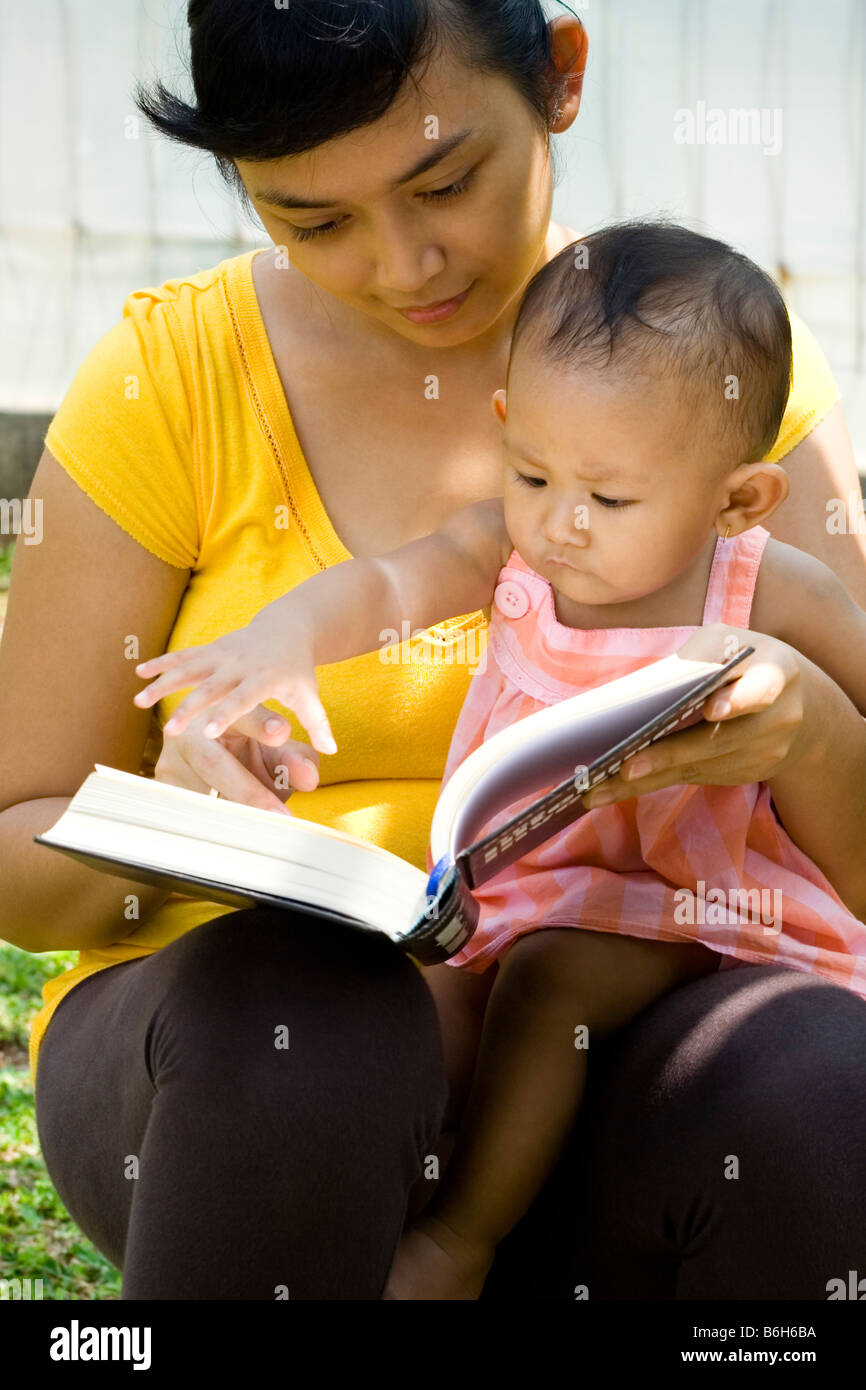 Young Southeast Asian Mother Reading a Book While Babysitting Her Baby ...