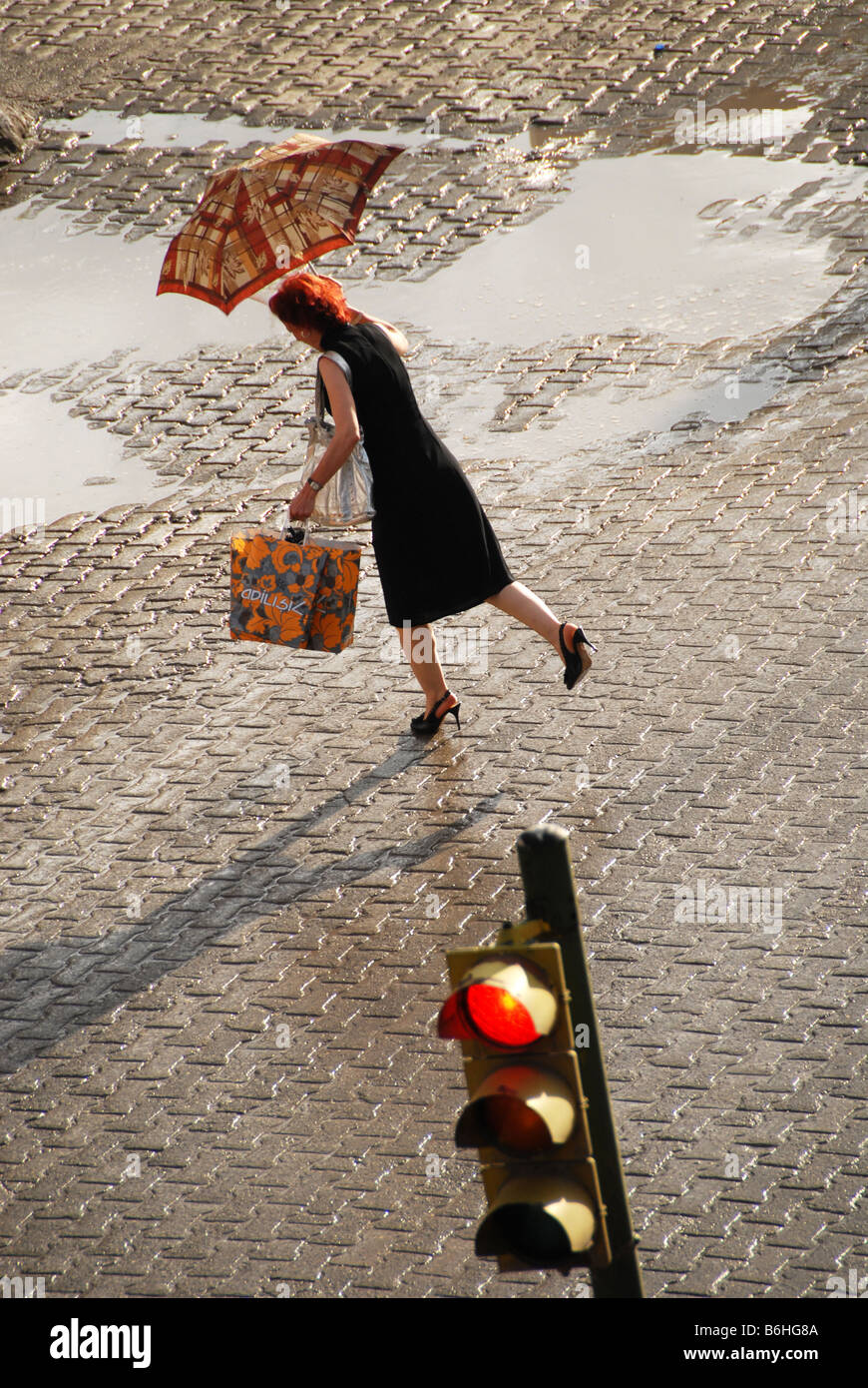 Woman crossing a street by a red traffic light, she is carrying an ...