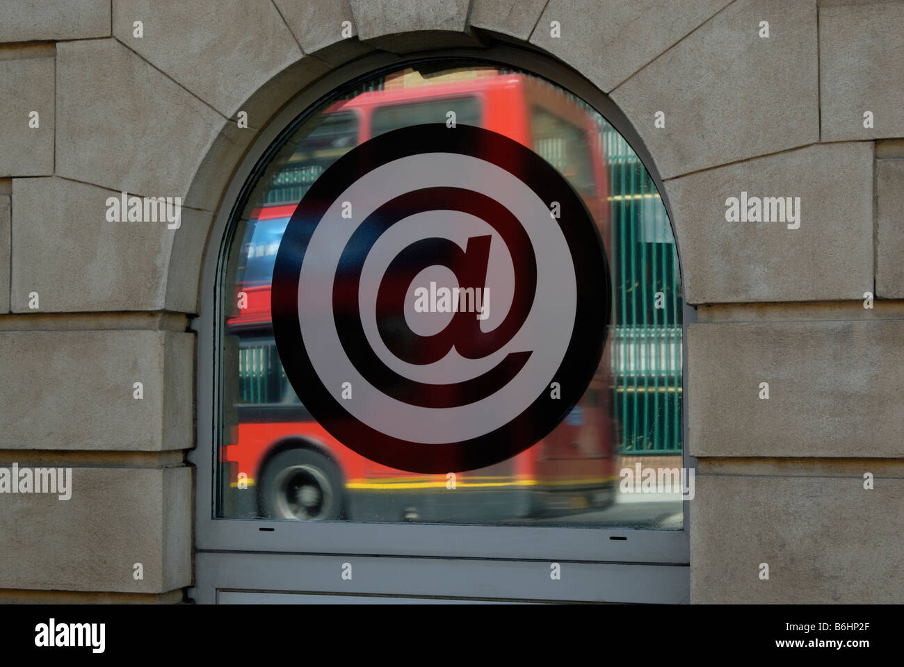 @ sign (at sign) on mirrored glass window with red doubledecker bus in ...