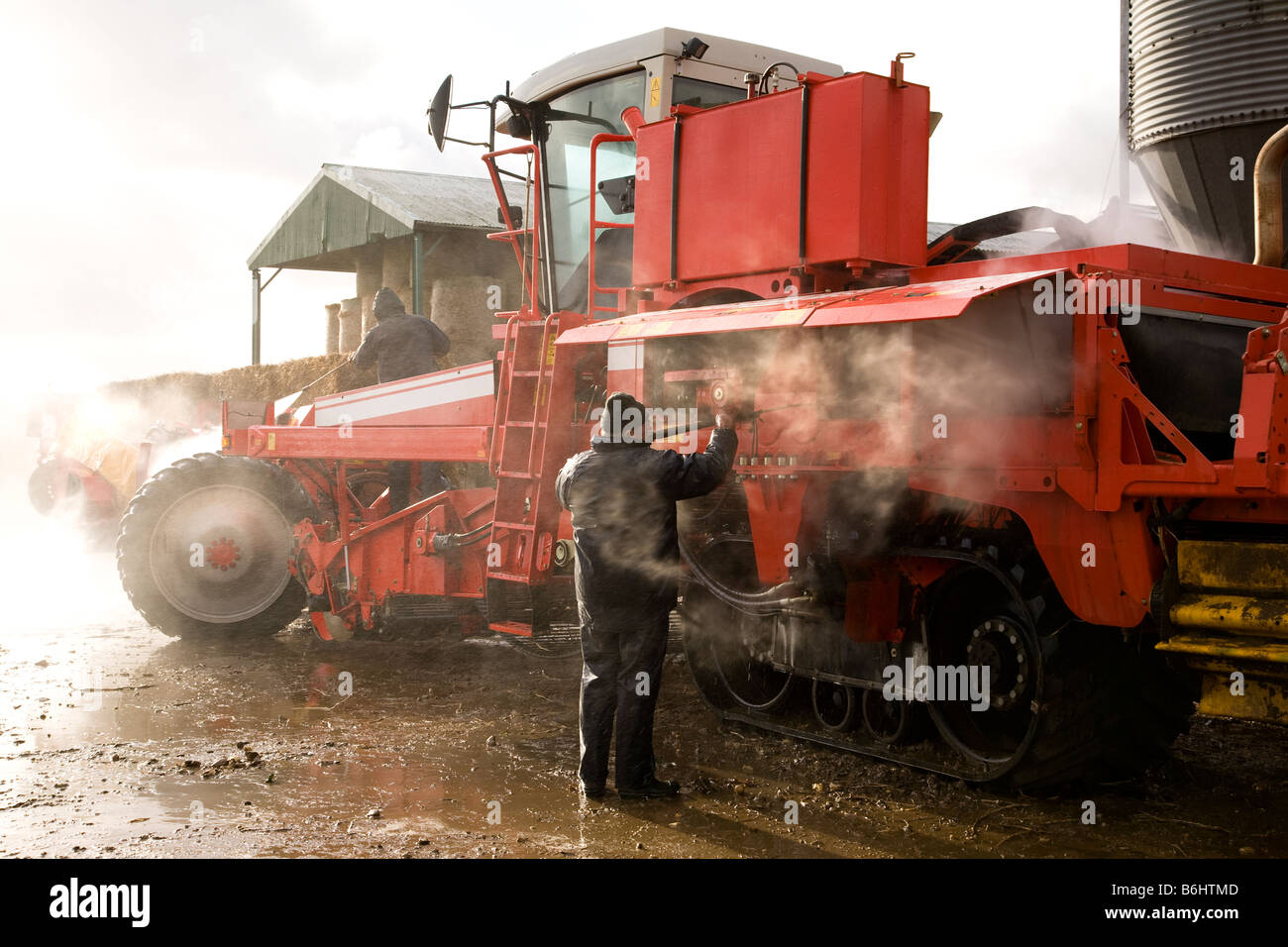 Two farmers pressure washing a potato harvester Stock Photo - Alamy