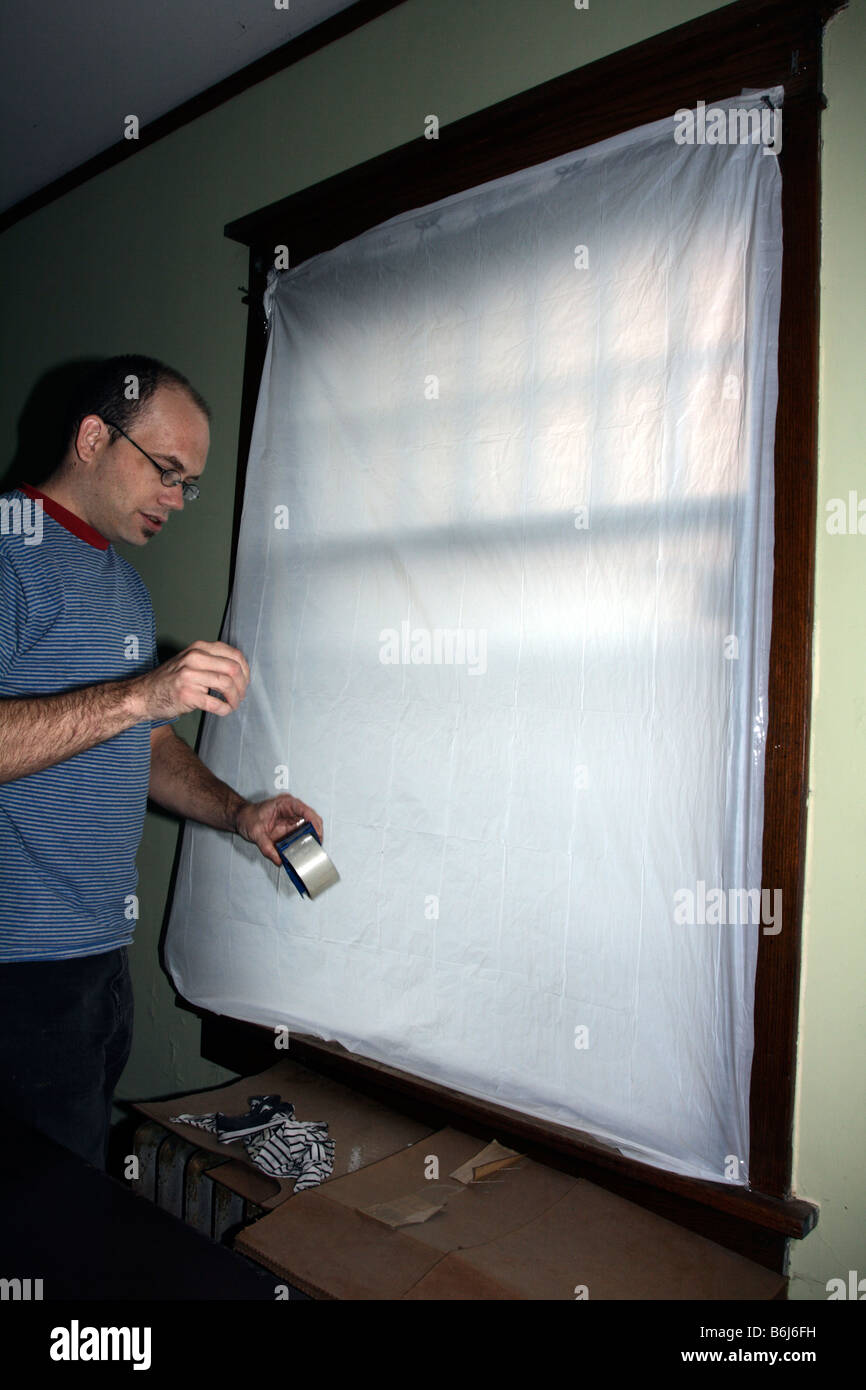Man with tape dispenser preparing to finish insulating a window with ...