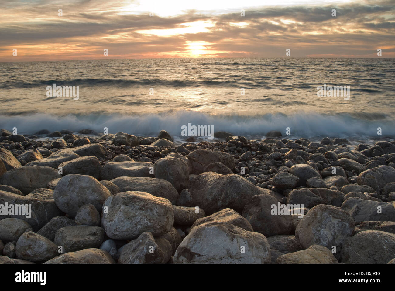 Sunset on a pebble beach Stock Photo - Alamy