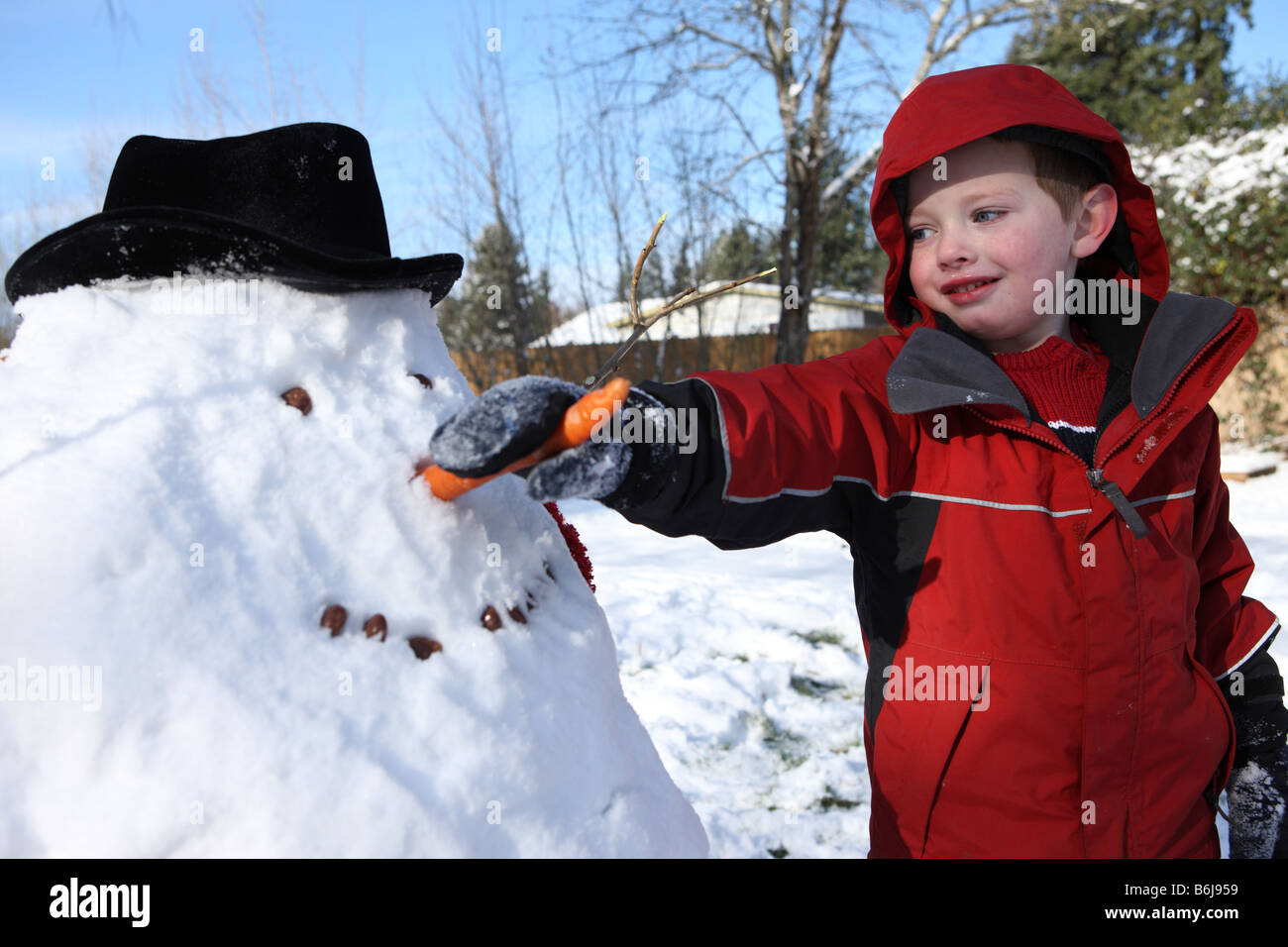 Young boy putting a carrot nose on a snowman Stock Photo - Alamy