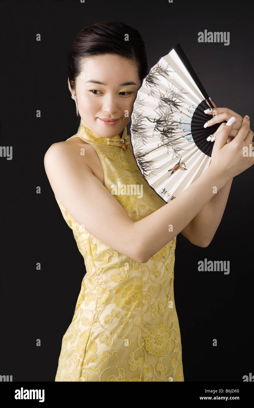 Young woman in yellow cheongsam holding folding fan Stock Photo - Alamy