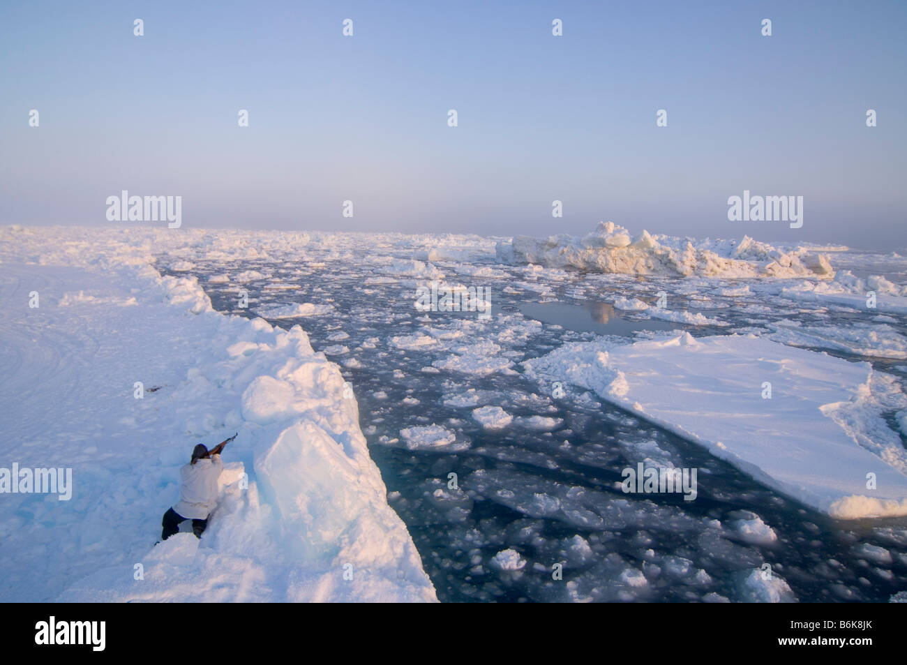 Inupiaq subsistence whaler aims his rifle at floating sea ice drifting ...