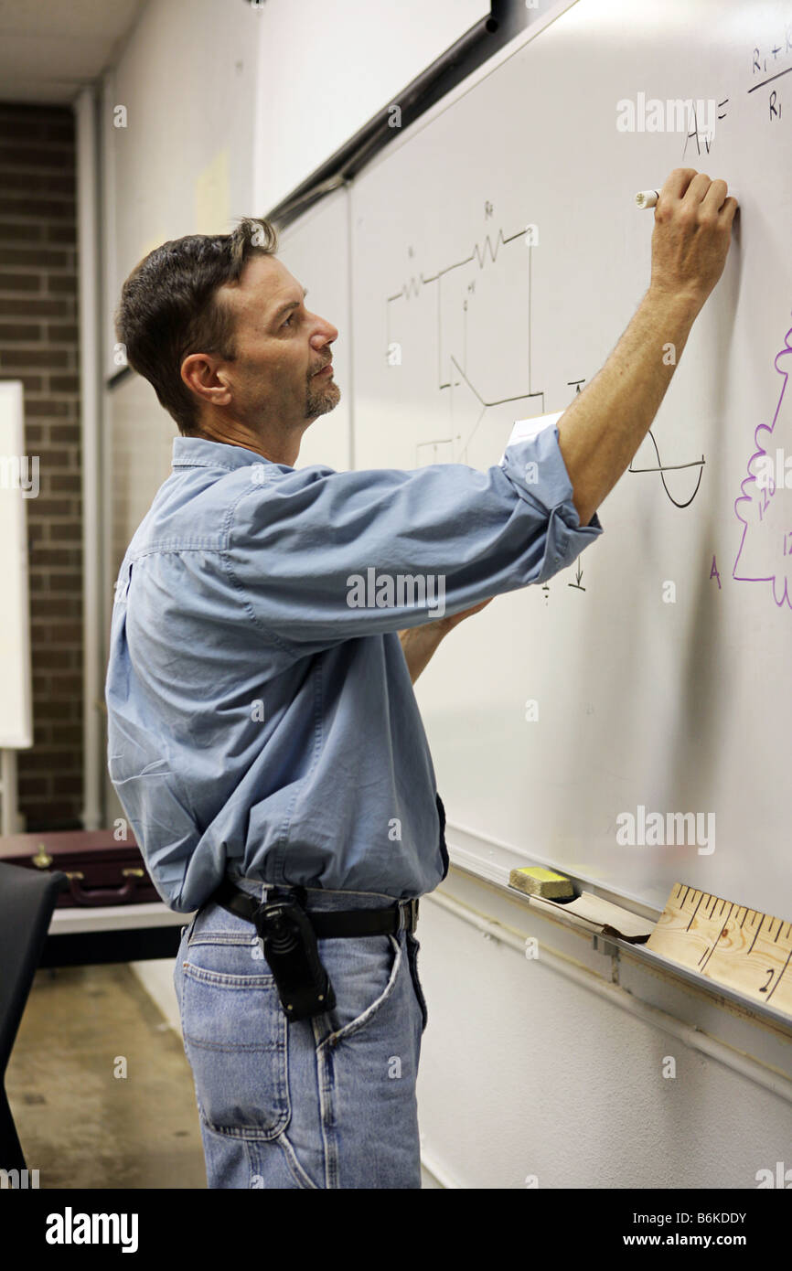 Handsome adult education teacher writing math problems on the board ...