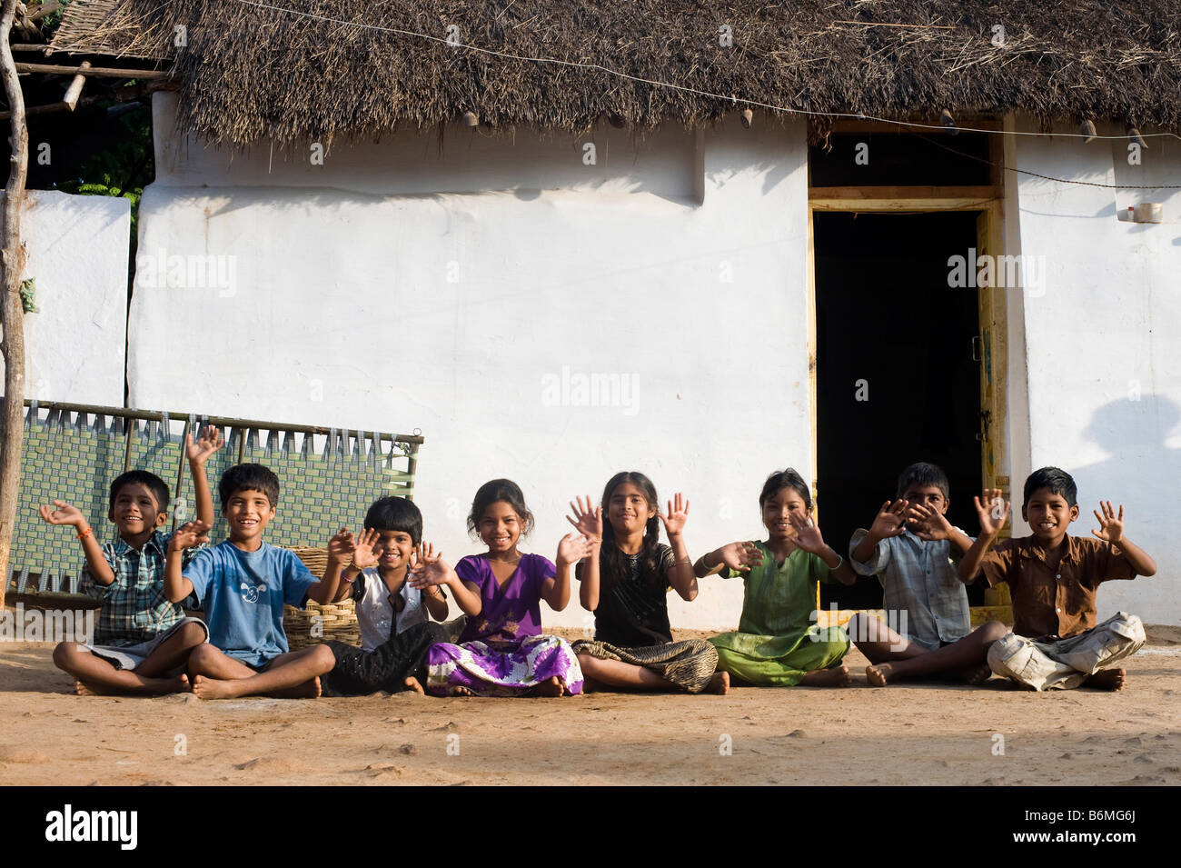 Indian children sitting in a row waving having fun outside a rural ...