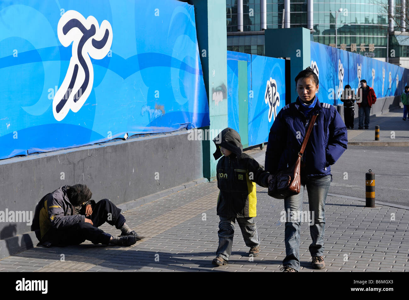 A poor man sits under a poster of the 2008 Beijing Olympic Games in ...