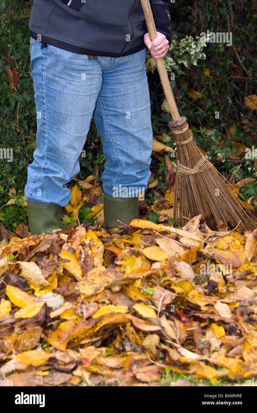 Young woman sweeping fallen autumn leaves with broom in back garden ...