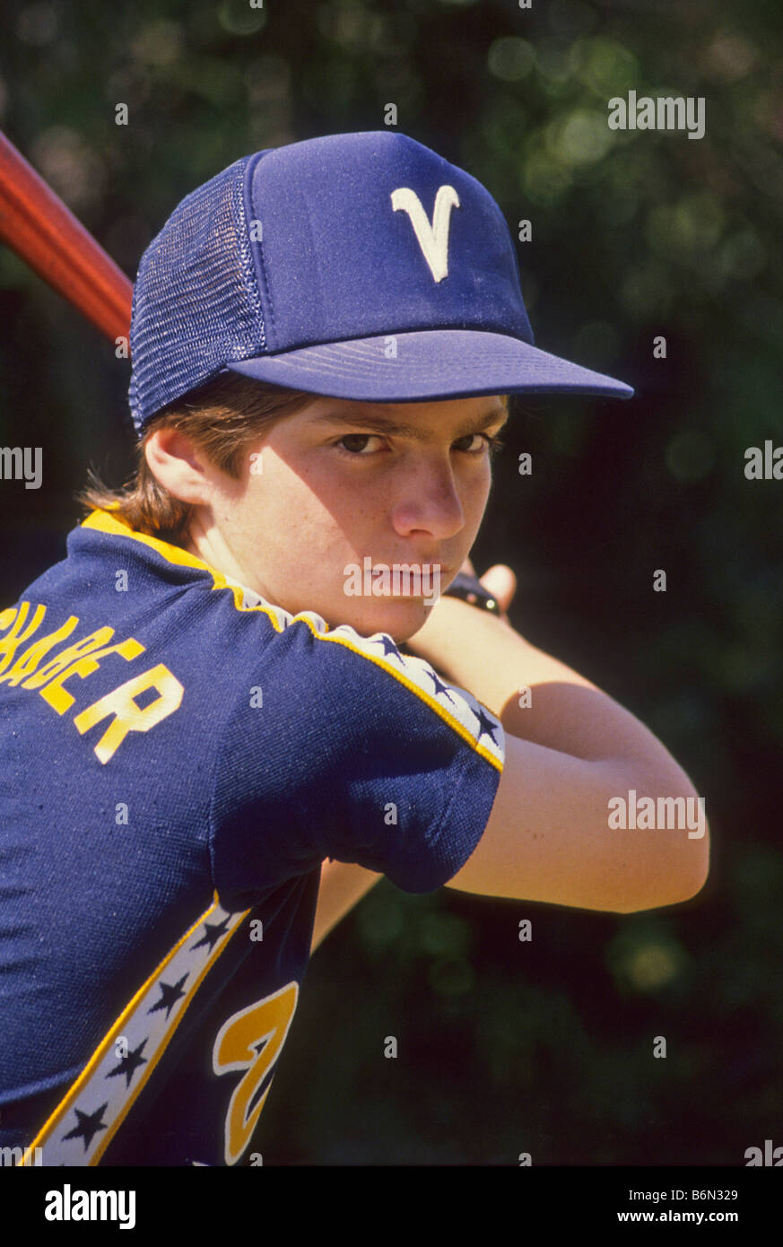 Teen boy holds bat over shoulder as he waits for the ball during ...