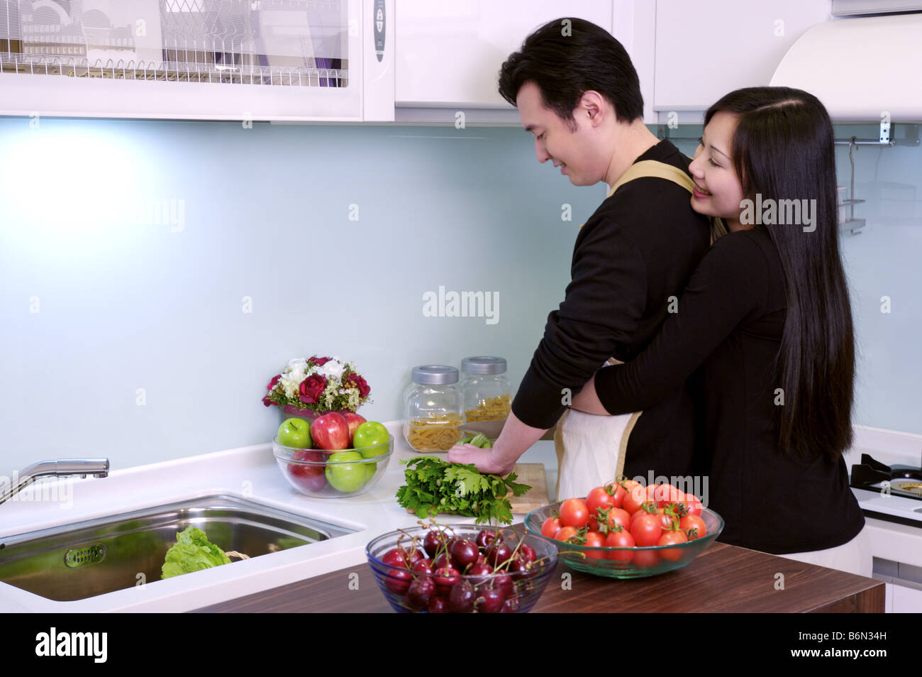 Woman hugging man as he prepares food in domestic kitchen Stock Photo ...