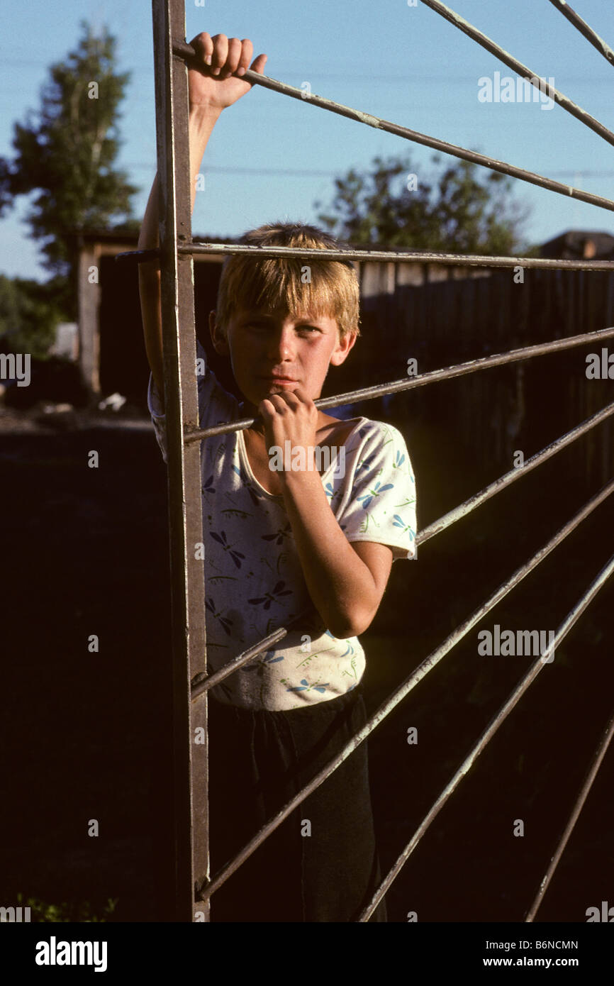 A young Siberian boy holds on to a gate while facing forward in late ...