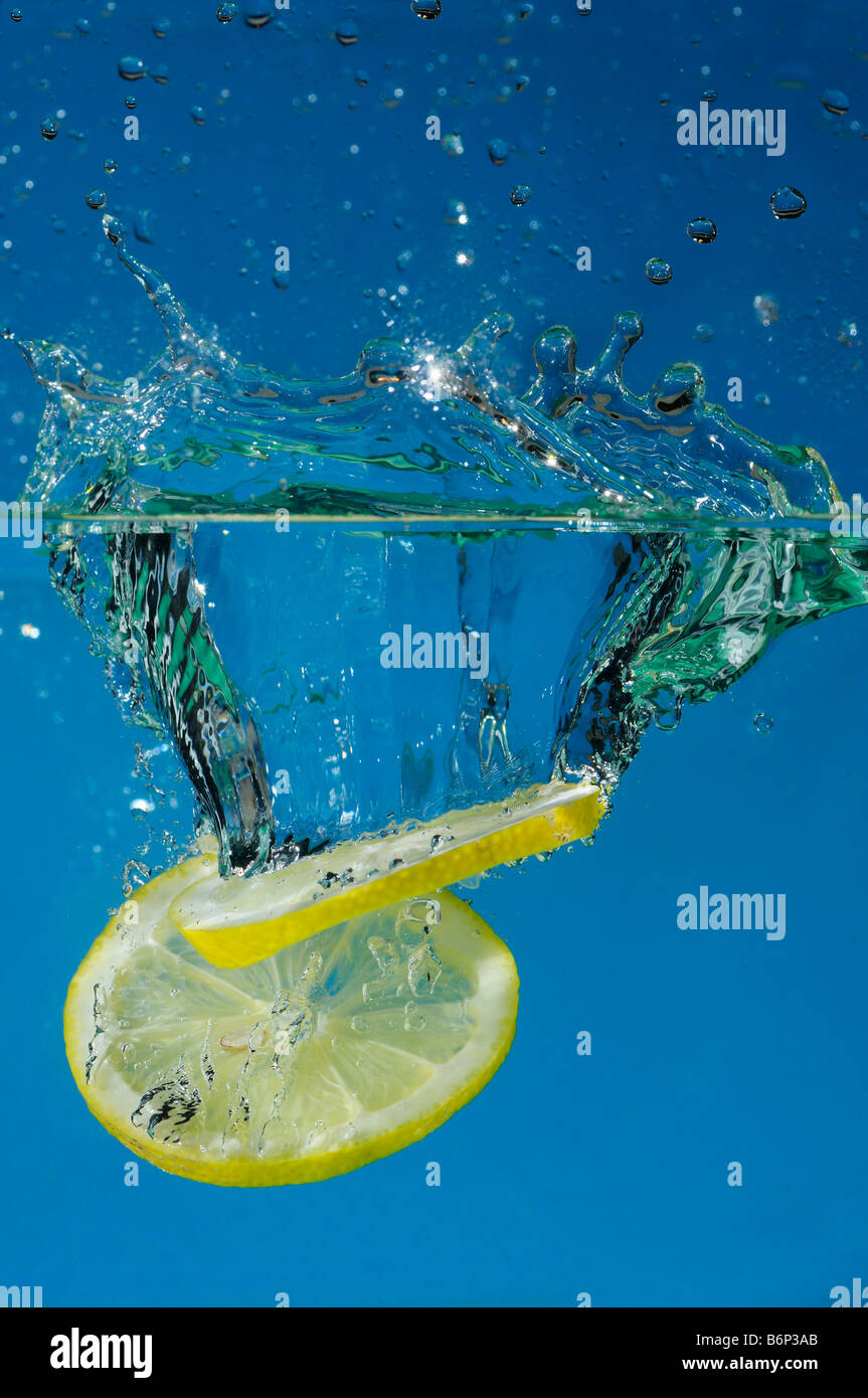 Pair of fresh lemon slices splashing into a water tank with a blue background Stock Photo - Alamy