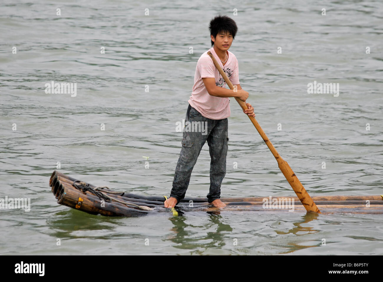 A Chinese man standing on a bamboo raft, Li river near Yangshuo ...