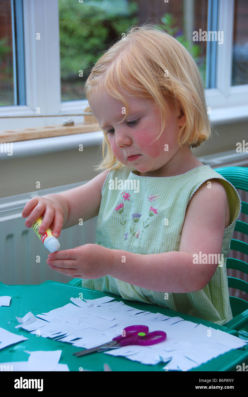 Little girl cutting and pasting paper shapes together in a conservatory ...