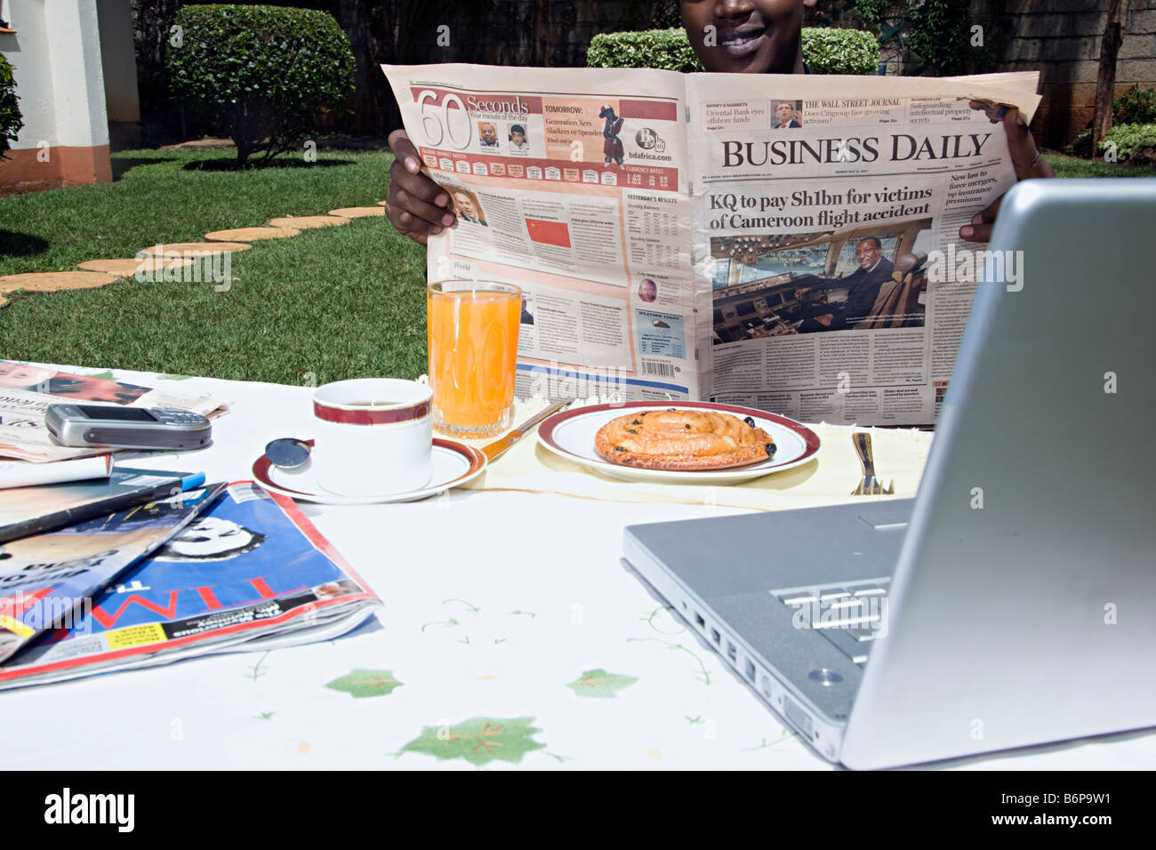 A businessman reading the daily newspaper at an outdoor breakfast table ...