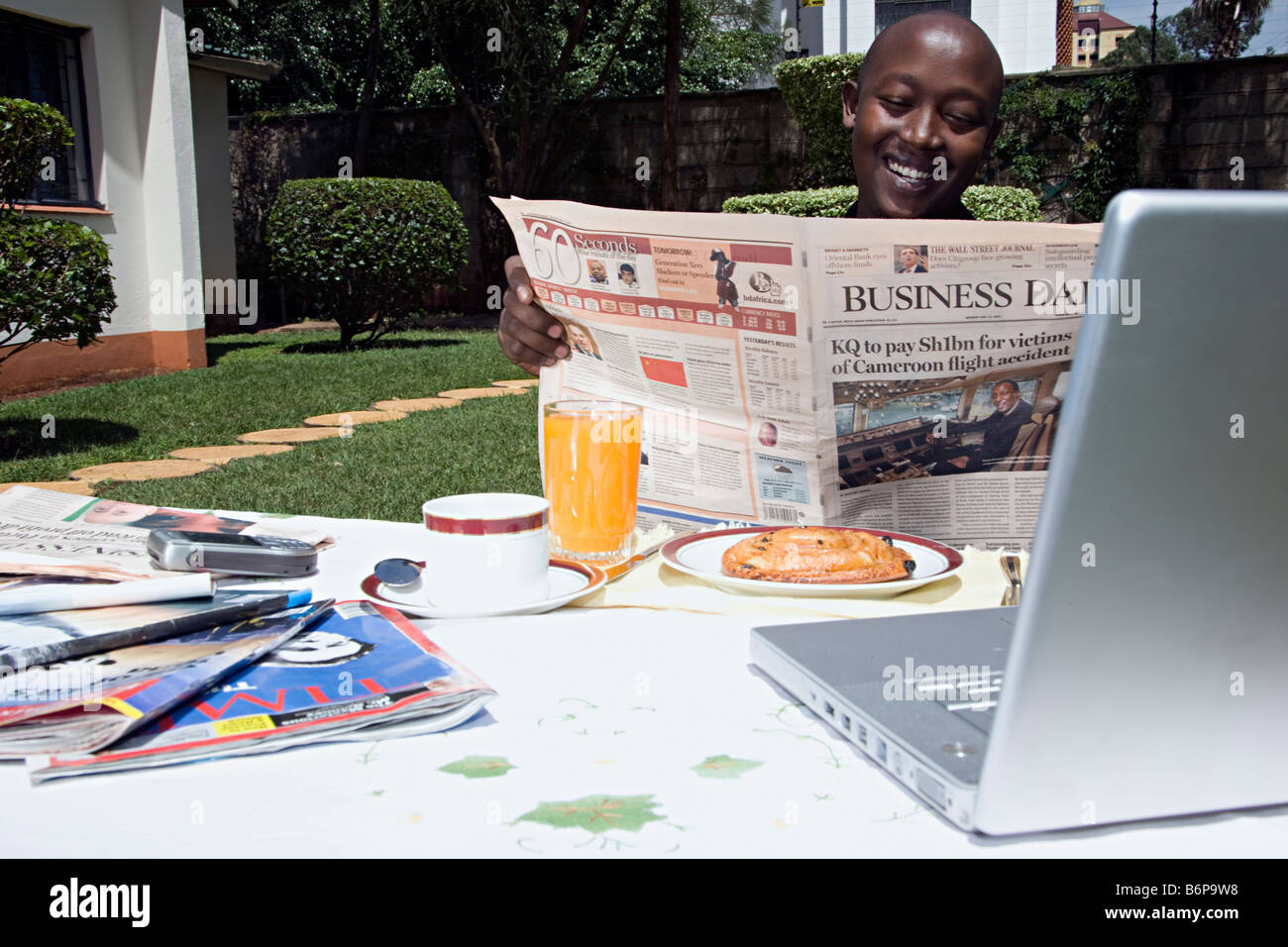 A businessman reading the daily newspaper at an outdoor breakfast table ...