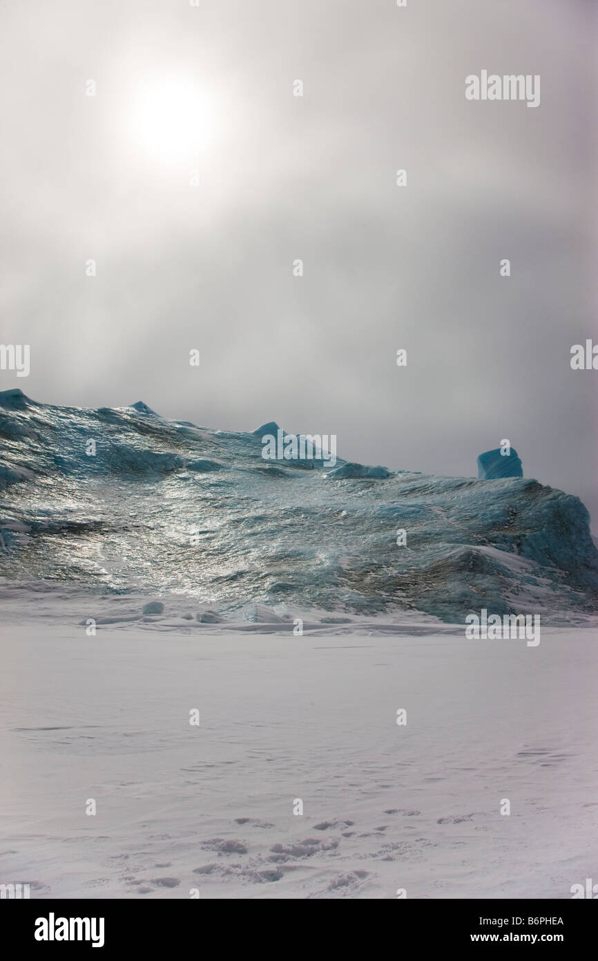 A blue iceberg locked in fast ice with the sun shining down through an ...