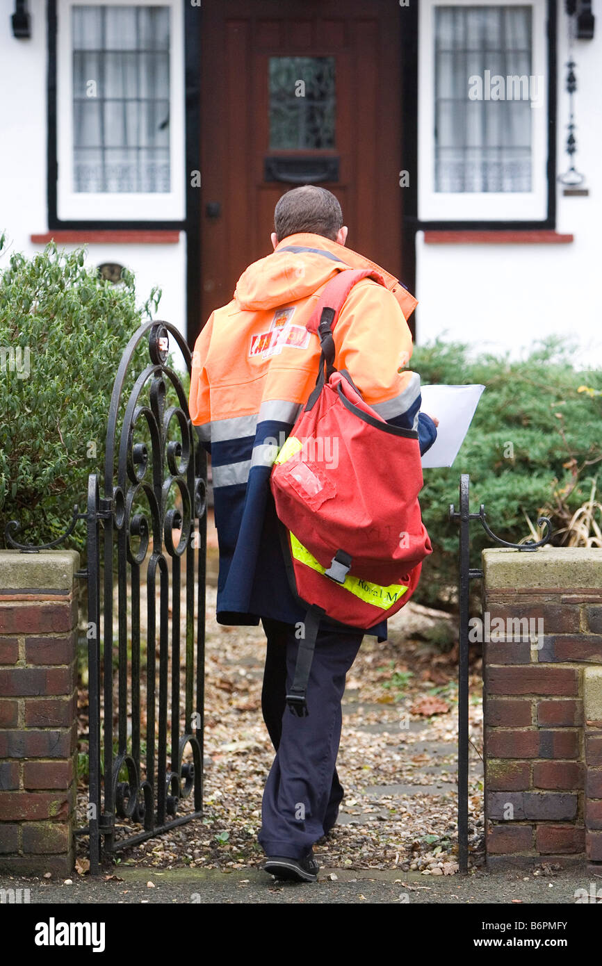 A Royal Mail postman walks up a path to deliver letters through a door ...