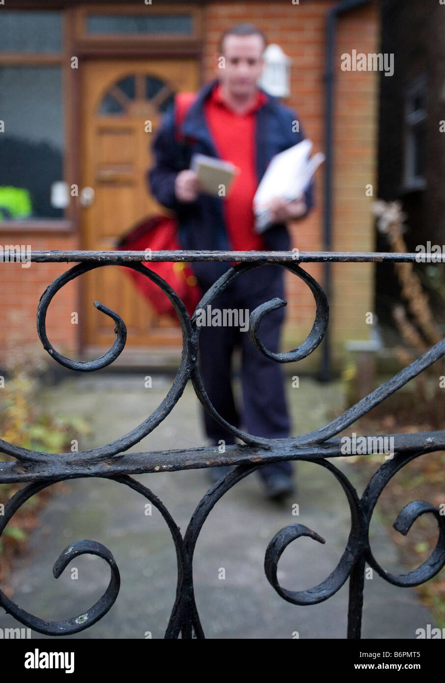 A Royal Mail postman walks up a path to deliver letters through a door ...