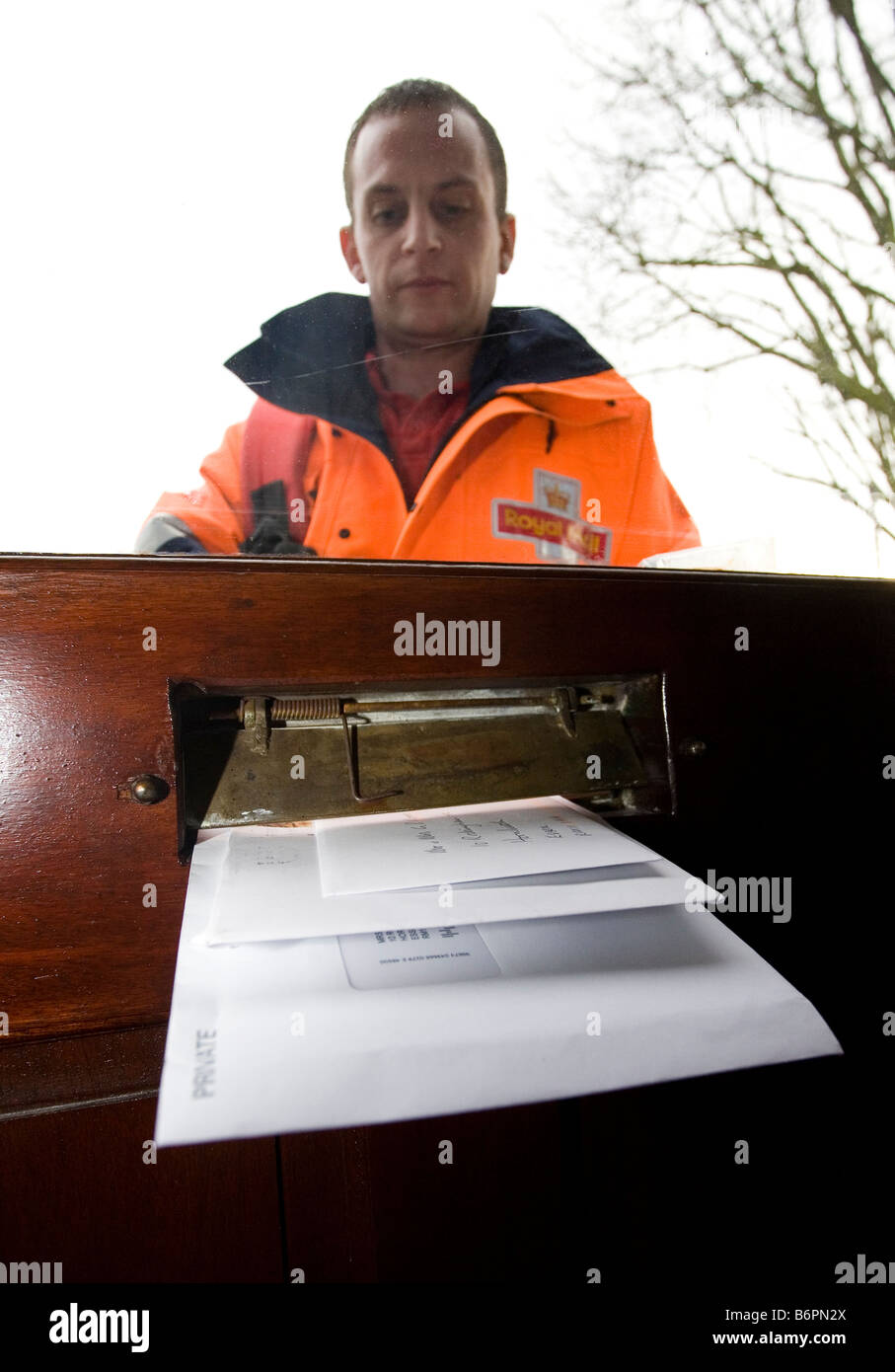 A Royal Mail postman delivers letters through a door on his round in ...