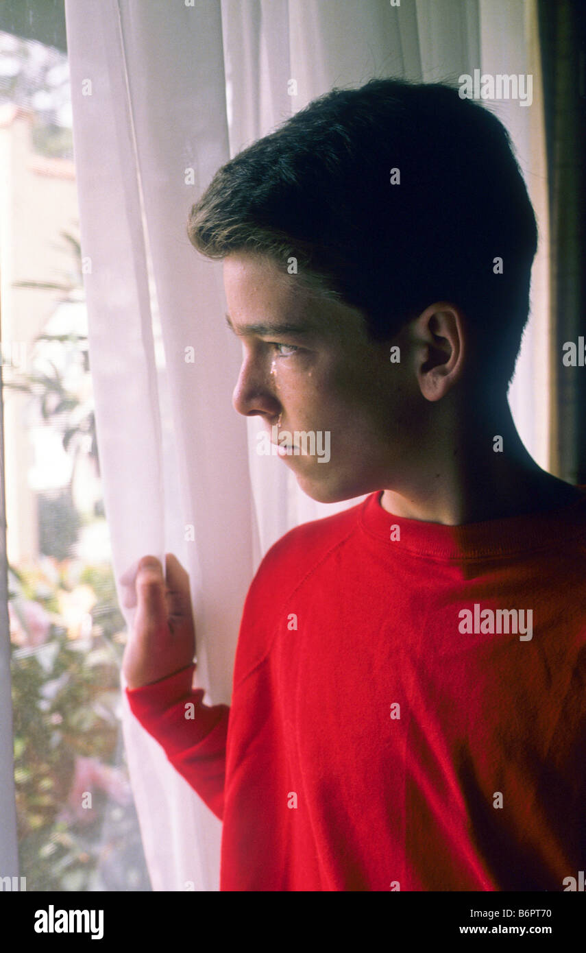 Teen boy with tears in eyes looks out of window Stock Photo - Alamy