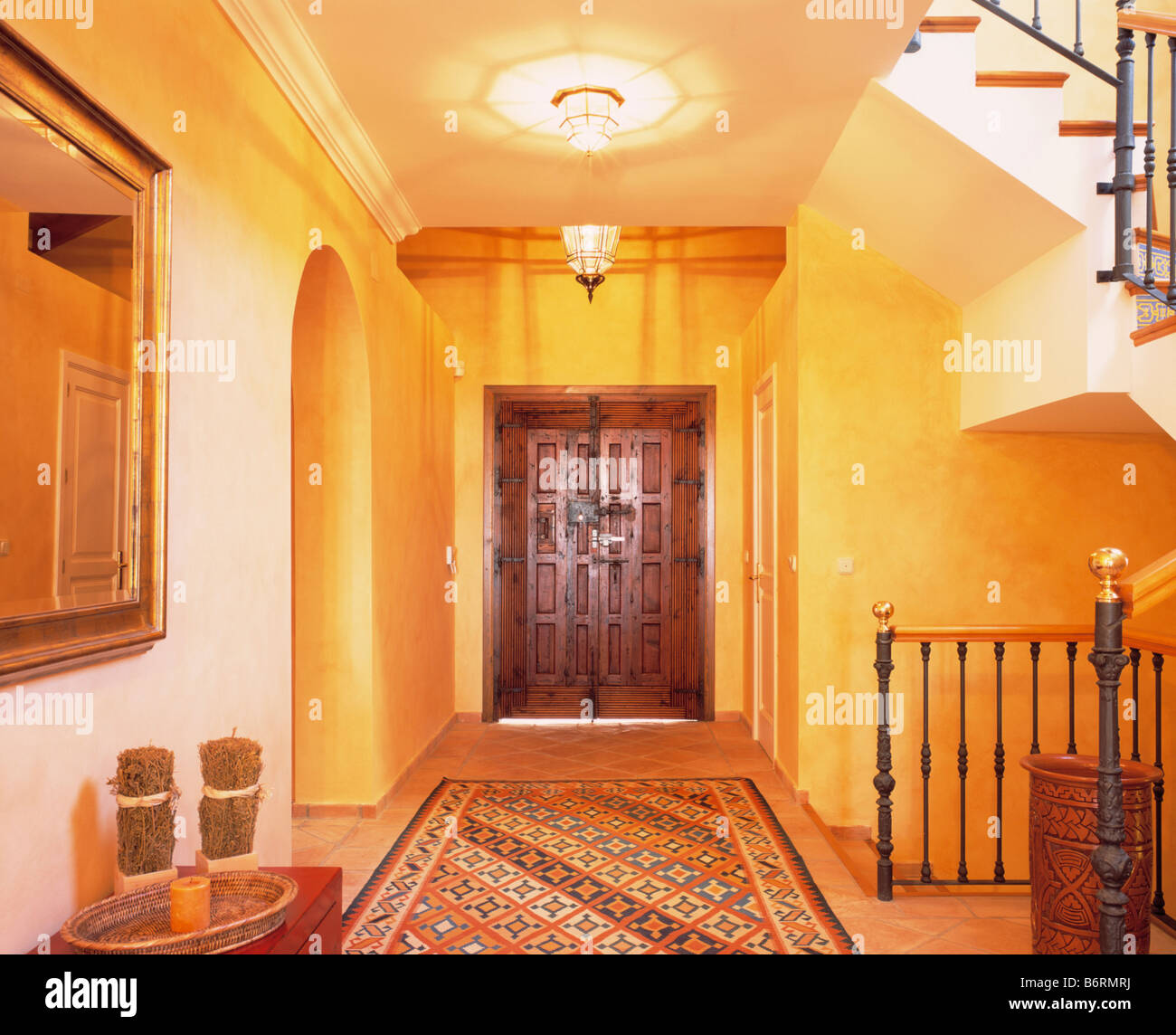Brightly patterned rug in yellow Spanish hall with carved wooden double ...